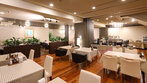 Ampla sala de jantar de hotel com várias mesas e cadeiras, espaço para buffet e design de teto moderno.