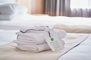 Uma pilha de toalhas brancas dobradas com um cartão verde sobre a cama.