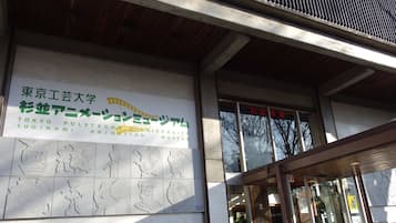 Entrada do Museu de Animação Suginami da Universidade Politécnica de Tóquio, com uma grande placa e diversos esboços artísticos na parede.