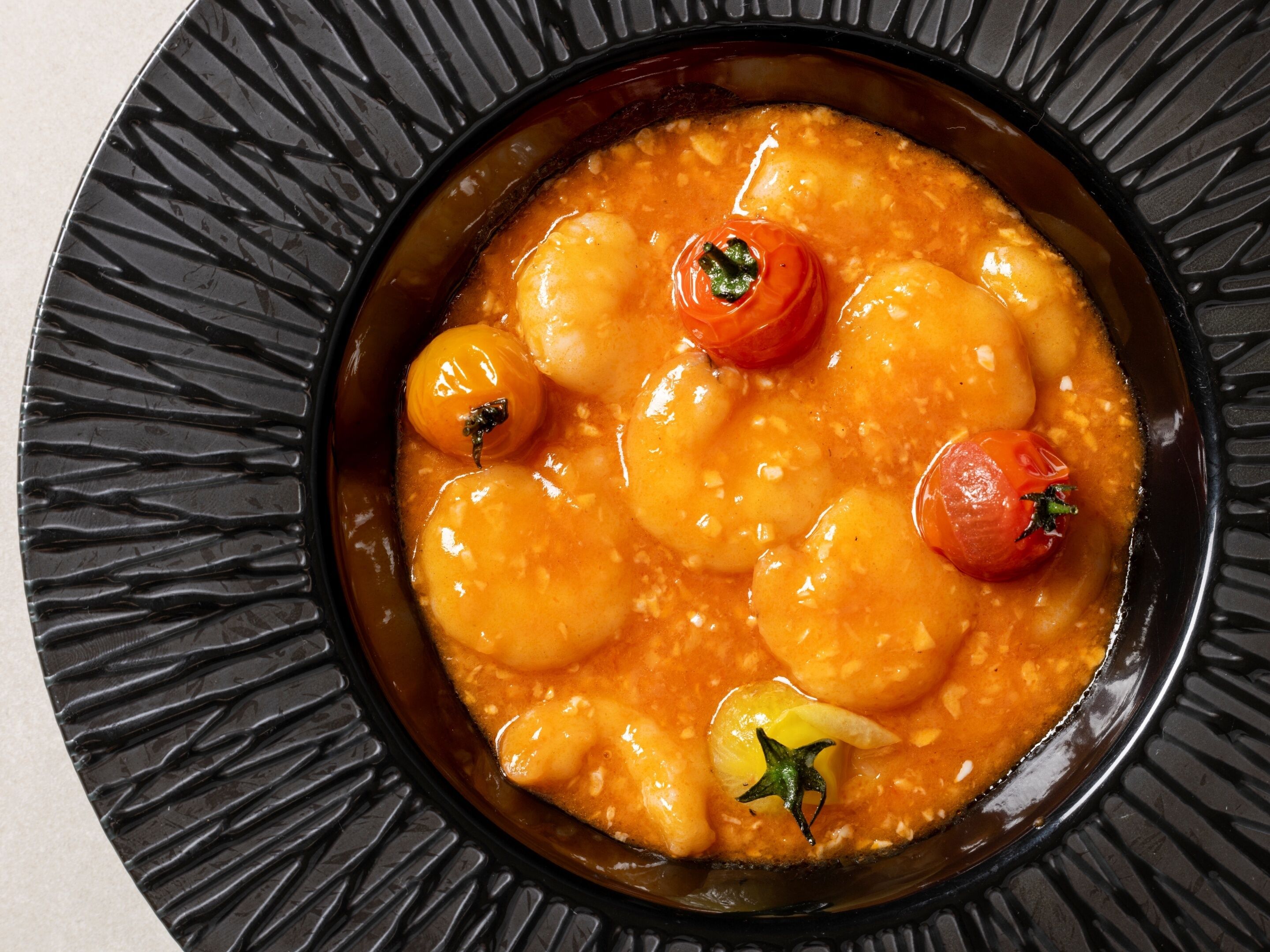 Uma tigela de sopa com tomates e um enfeite, servida em uma tigela preta sobre uma superfície texturizada.