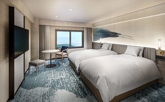 Quarto de hotel com uma cama grande, televisão, mesa pequena e janela com vista.