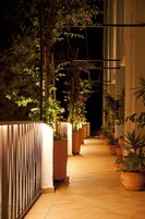 Corredor com plantas em vasos, piso de azulejos e corrimão de metal.