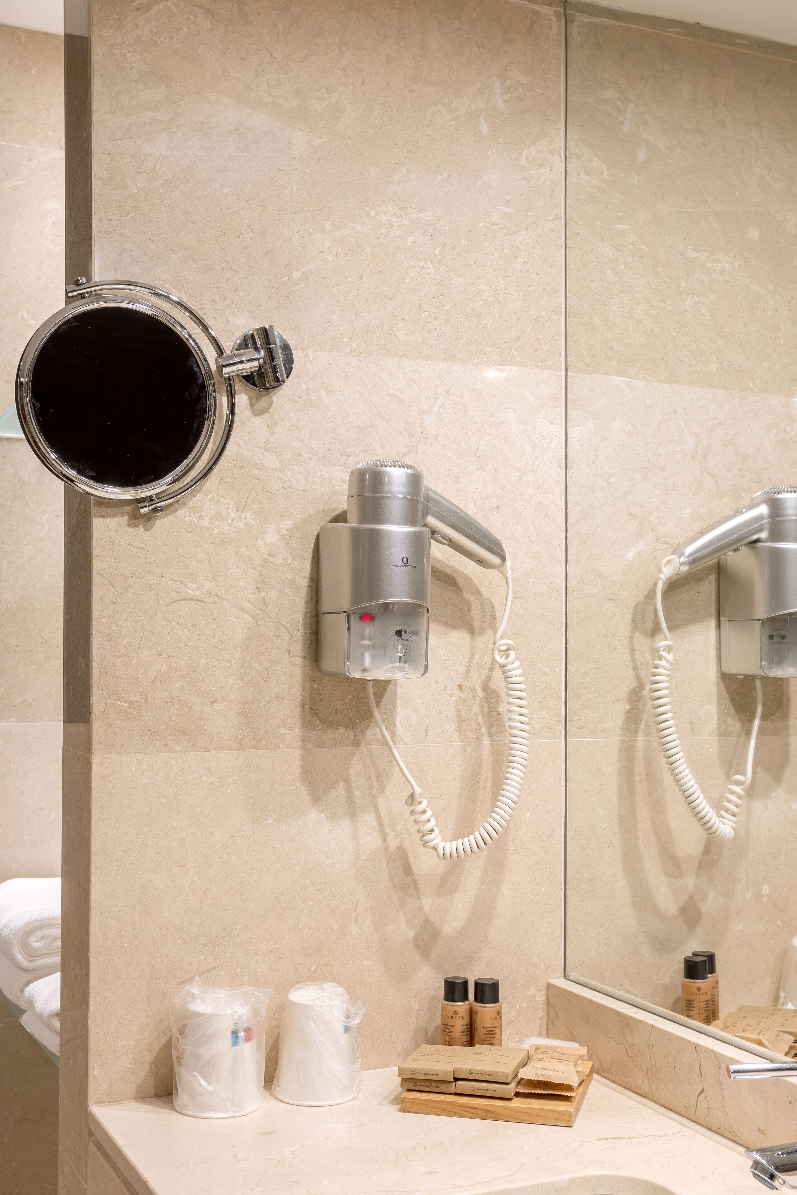 Casa de banho com secador de cabelo fixado na parede, espelho e artigos de higiene no lavatório.