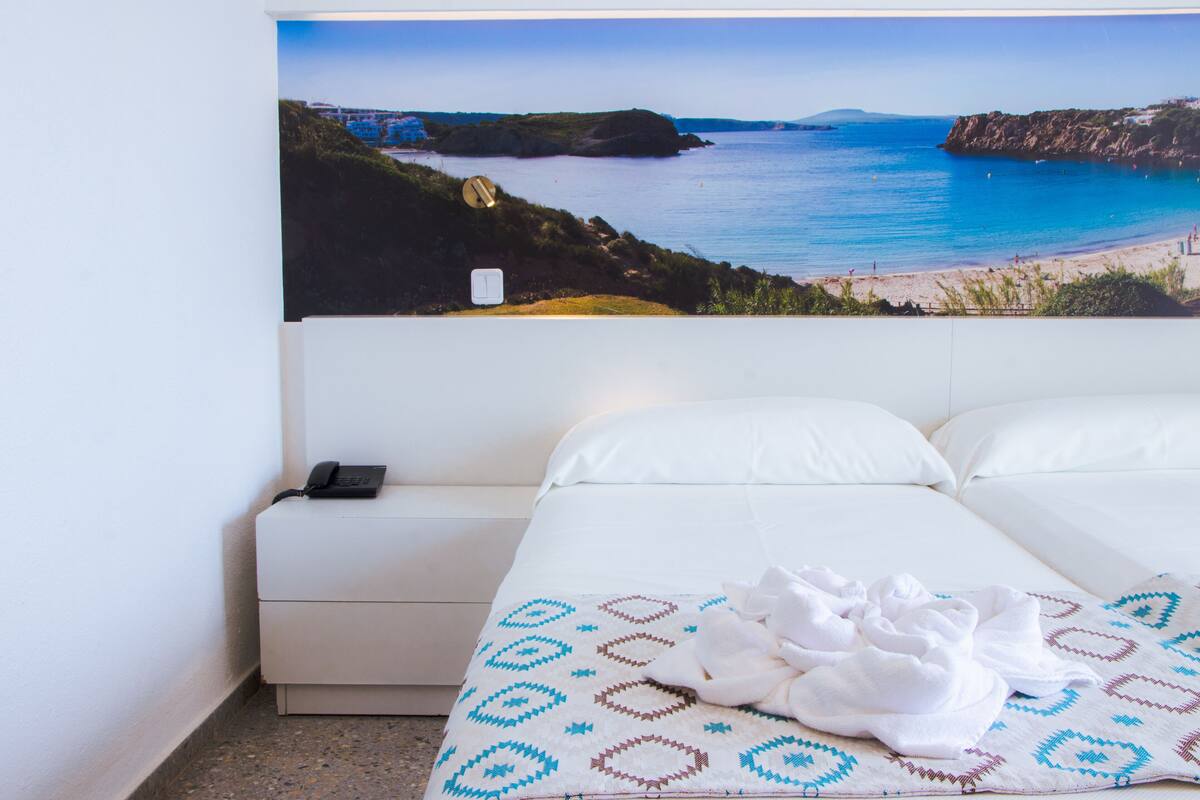 Quarto de hotel com uma cama, um sofá branco e um grande mural panorâmico na parede.