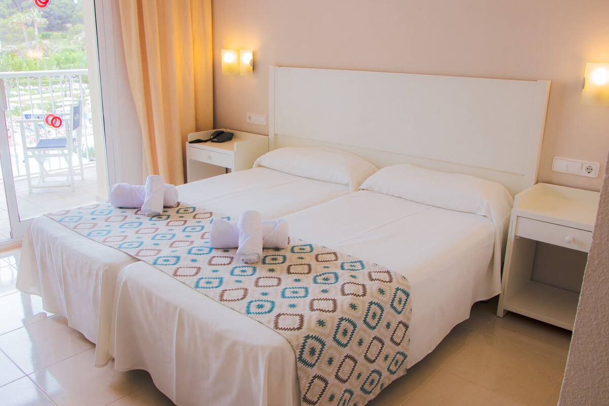Quarto de hotel com duas camas, varanda e vista para o exterior.