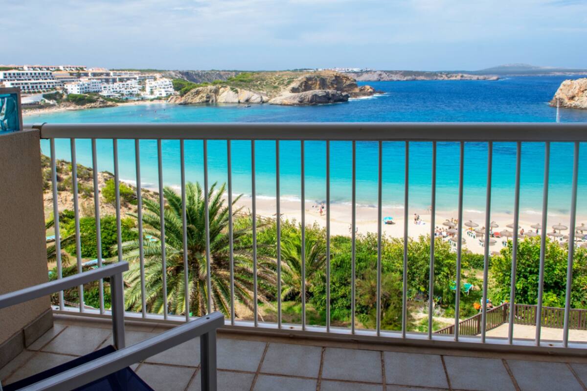 Uma varanda com vista para uma praia, palmeiras e um litoral rochoso.