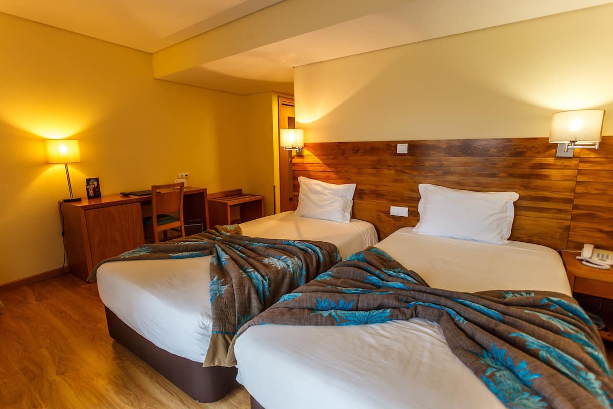 Quarto de hotel com duas camas, uma mesa e uma cadeira.