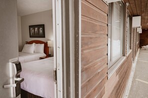 Quarto de hotel com duas camas, parede de madeira e uma janela.