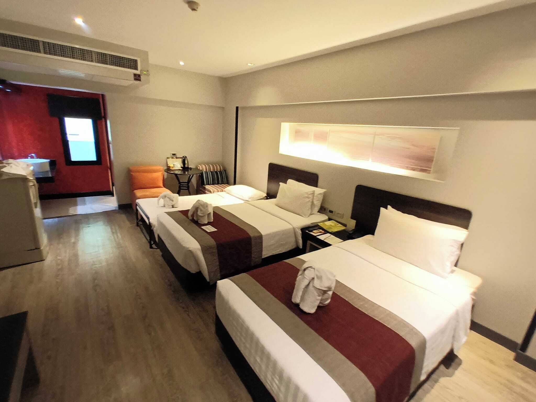 Quarto de hotel com três camas, uma escrivaninha e uma cadeira.