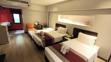 Quarto de hotel com três camas, uma escrivaninha e uma cadeira.