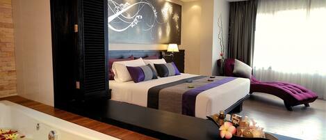 Quarto de hotel moderno com uma cama grande, área de estar e banheira com pétalas de rosa.