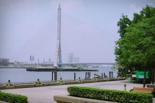 Um calçadão à beira-mar com um monumento imponente, bancos e vista para uma ponte ao fundo.