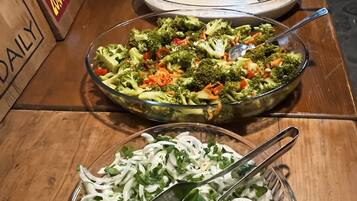 Mesa de buffet com diversos pratos, incluindo saladas, legumes e um letreiro com o menu diário.