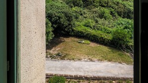 Vista da janela sobre paisagem costeira com praia, vegetação densa e céu claro.
