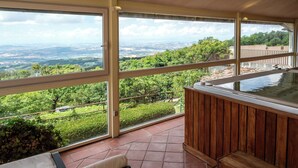 Uma varanda com banheira de hidromassagem, janelas amplas e vista para uma paisagem verde.