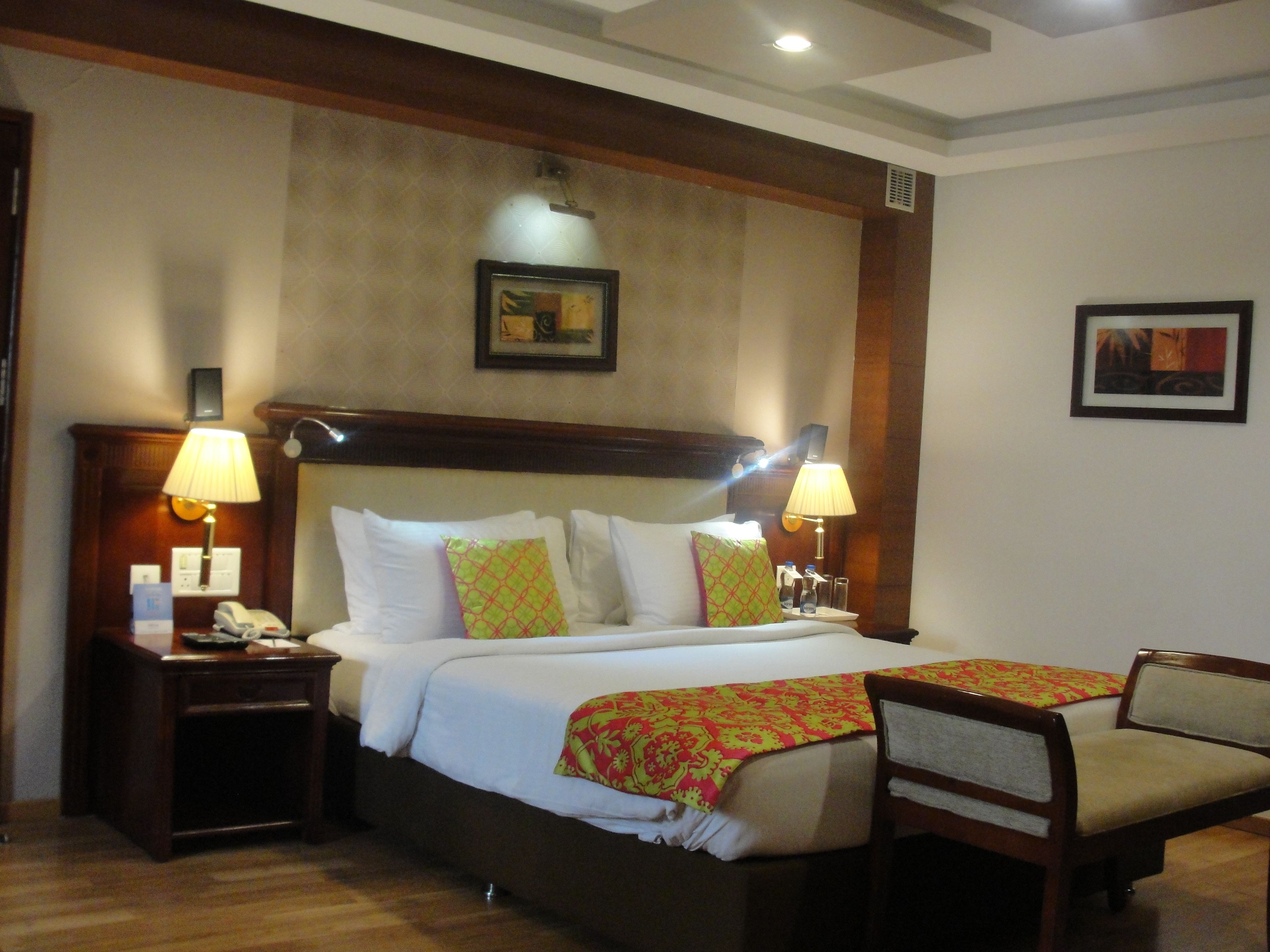 Quarto de hotel com uma cama grande, duas luminárias de cabeceira, mesa de apoio com telefone e uma cadeira.