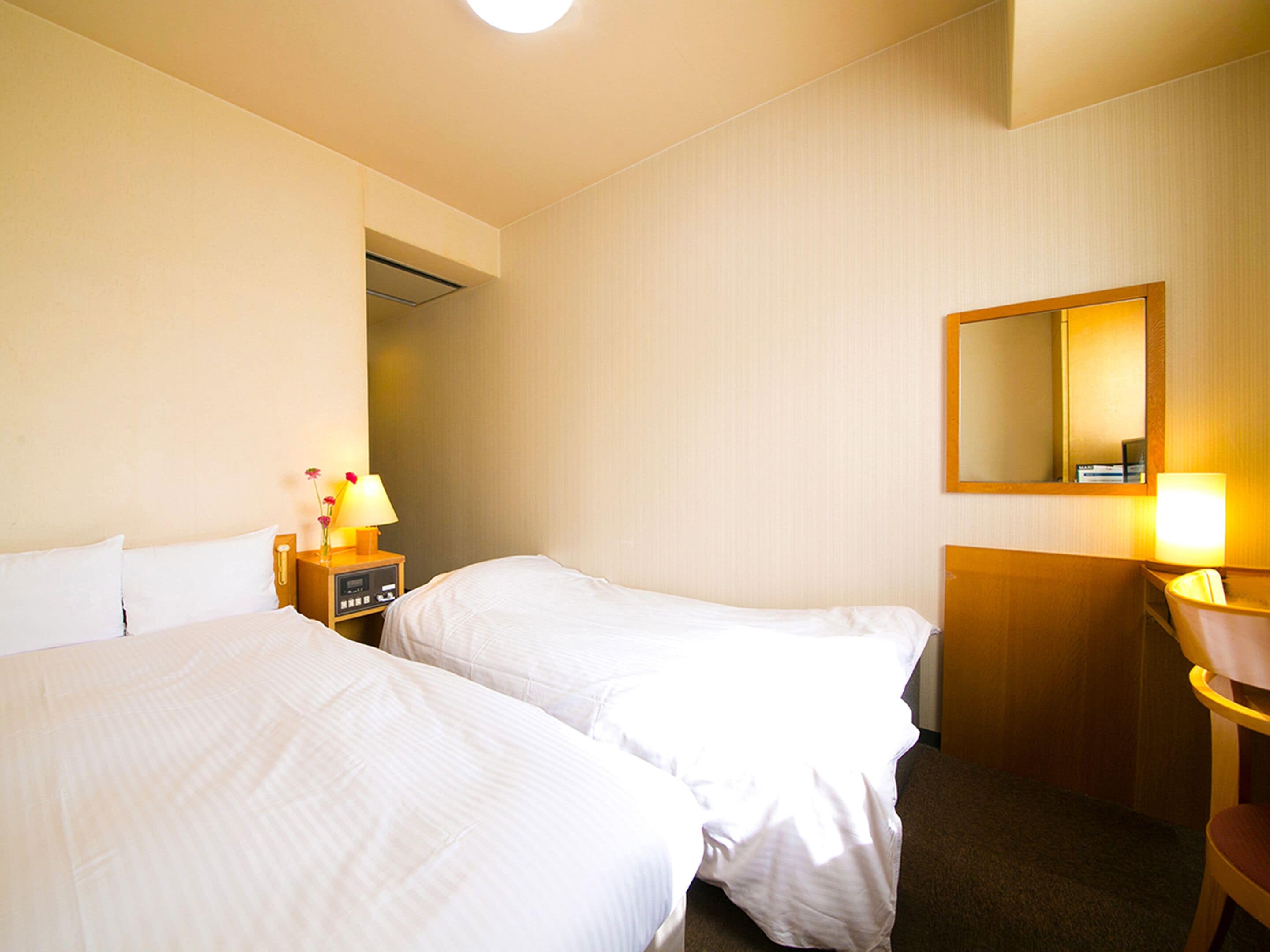 Quarto de hotel com duas camas, mesa de cabeceira com luminária, um rádio e um espelho na parede.