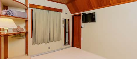 Quarto de hotel com cama, escrivaninha com luminária, guarda-roupa e janela com cortinas.