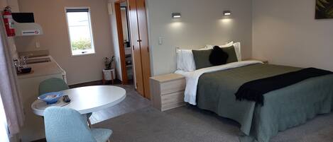 Quarto de hotel com cama, mesa de cabeceira, cadeira e uma pequena cozinha.