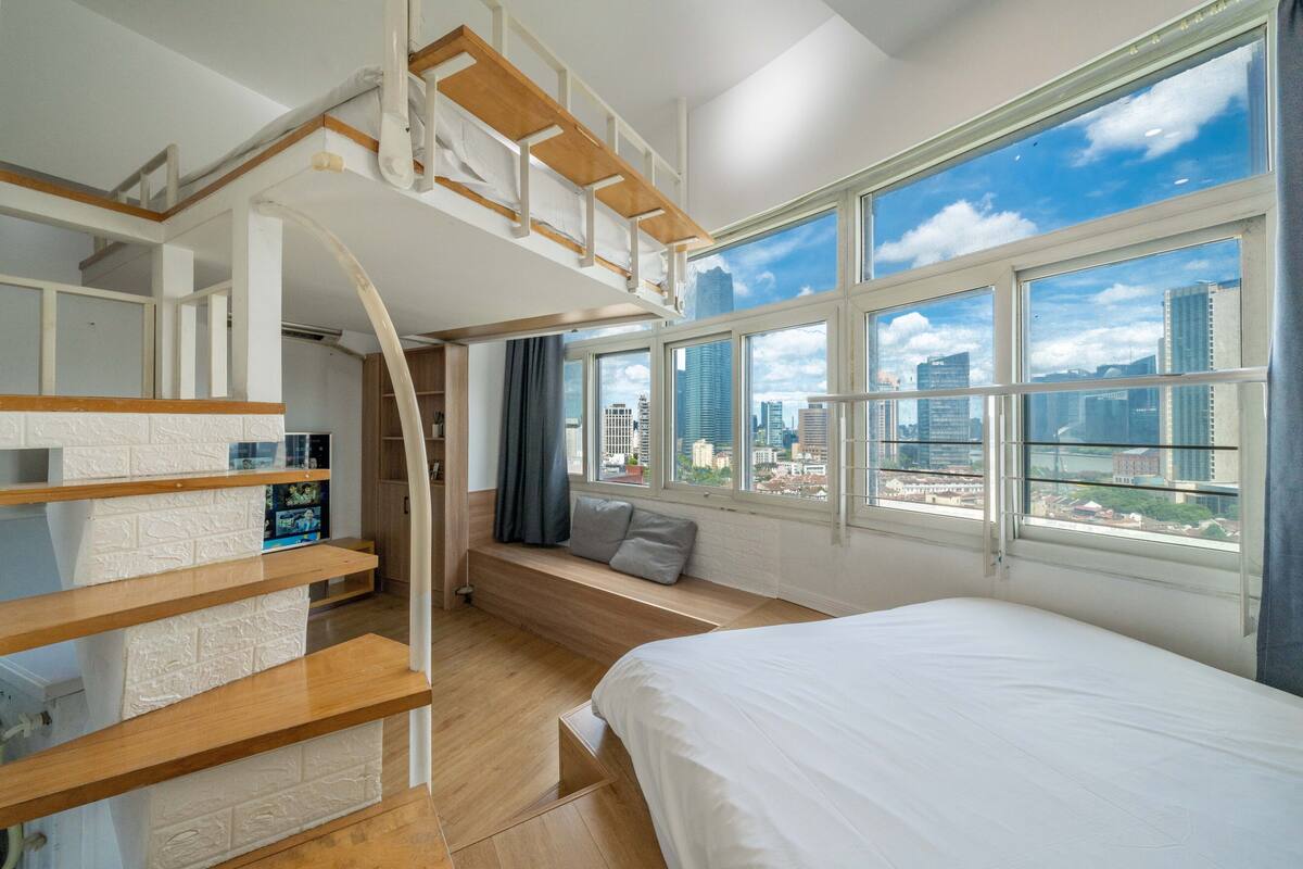Quarto moderno com área de dormir em mezanino, ampla janela com vista para a cidade e um banco embutido com espaço de armazenamento.
