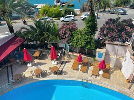 Uma área à beira da piscina com espreguiçadeiras e guarda-sóis, piscina e vista para o mar com barcos.