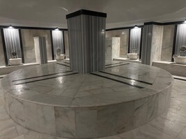 Um saguão circular em mármore, com uma coluna central, piso de mármore e luminárias modernas.
