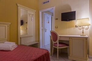Quarto de hotel com cama, escrivaninha, cadeira, televisão e abajur.