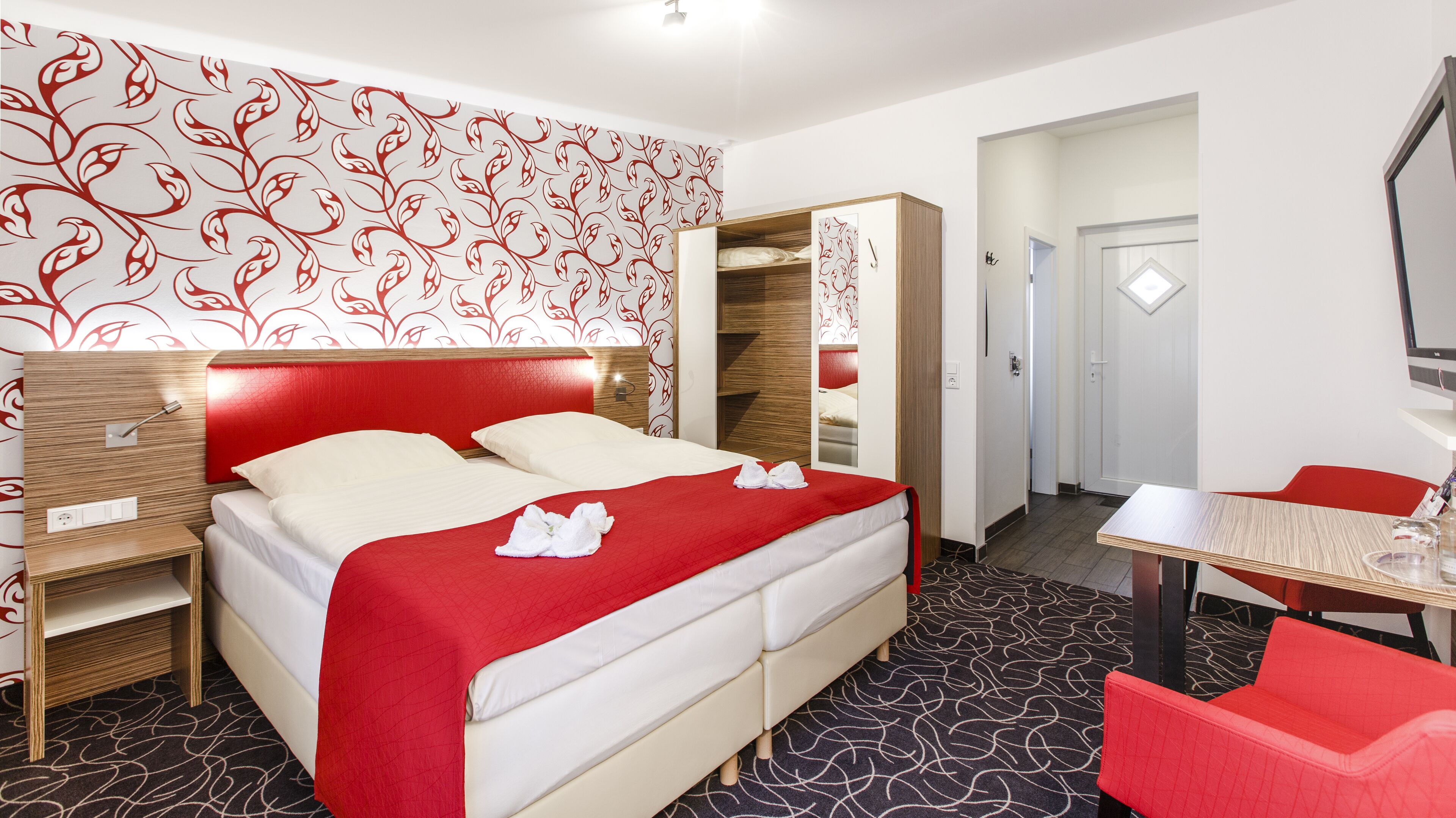 Quarto de hotel com cama, escrivaninha, guarda-roupa e espelho.