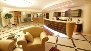 Um saguão de hotel com uma recepção em curva, um sofá e uma planta em vaso.