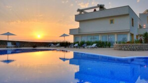 Um hotel moderno com piscina, espreguiçadeiras e vista para o pôr do sol.