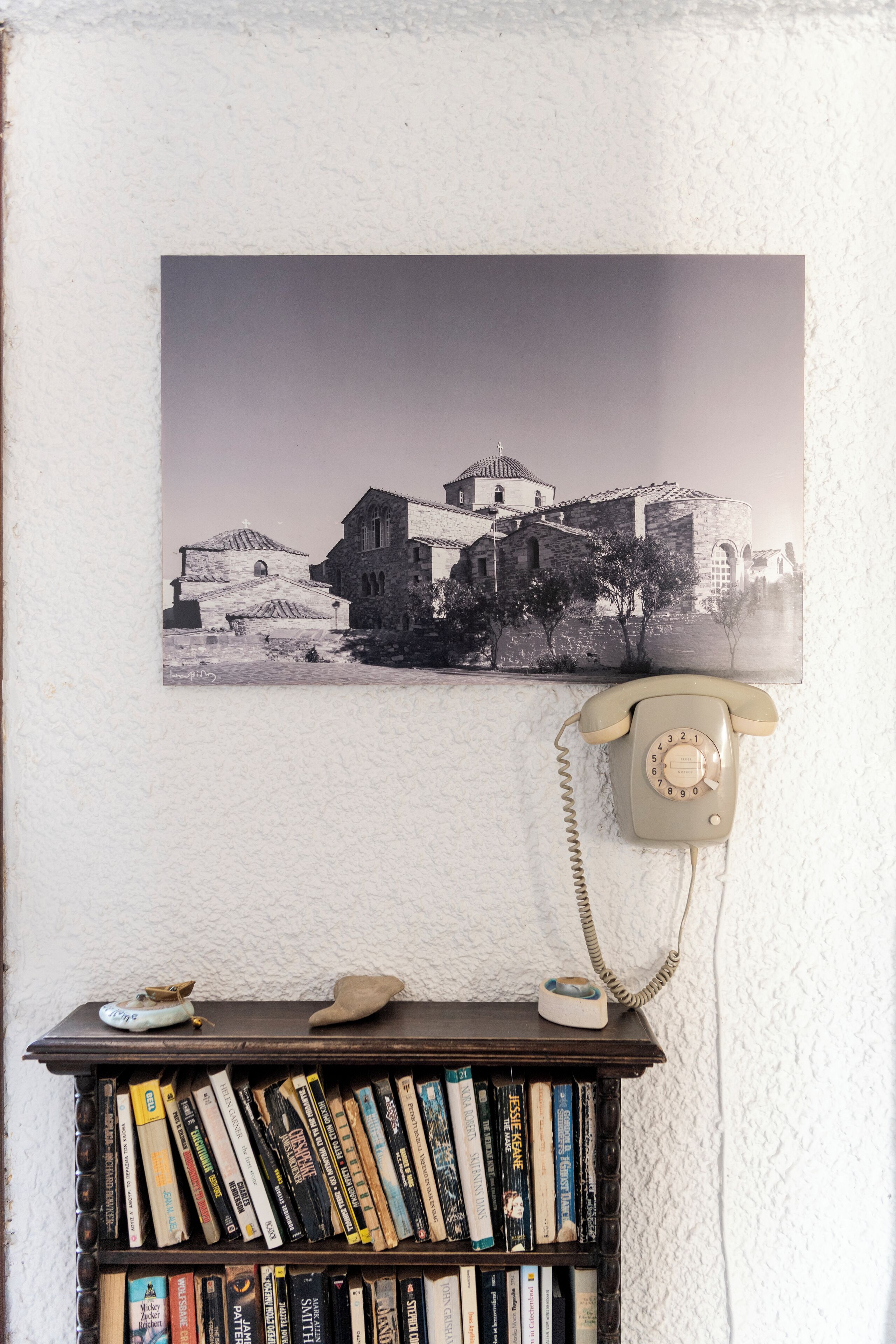 Um telefone antigo, uma estante com livros e um quadro emoldurado na parede.