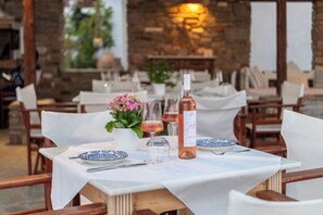 Um restaurante com mesas preparadas para refeições, com toalhas de mesa brancas, cadeiras de madeira e uma parede de pedra ao fundo.