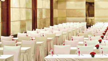 Salão de banquetes com fileiras de mesas montadas para um evento formal, com toalhas de mesa brancas e cadeiras.