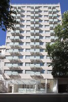 Um edifício de vários andares com design arquitetônico moderno, com várias varandas e entrada no nível da rua com portas de vidro.