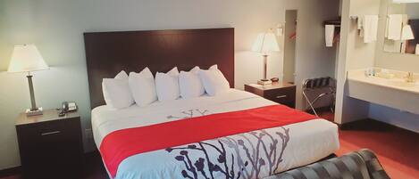 Quarto de hotel com uma cama grande, duas mesas de cabeceira com luminárias, uma poltrona, um sofá e um banheiro com pia e espelho.