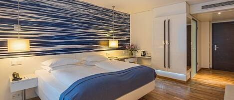Quarto de hotel moderno com uma cama grande, mesas de cabeceira, um guarda-roupa e uma parede com um padrão de luz único.