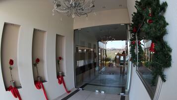Um saguão de hotel com entrada de vidro, rosas vermelhas em vasos, um candelabro e uma árvore de Natal.