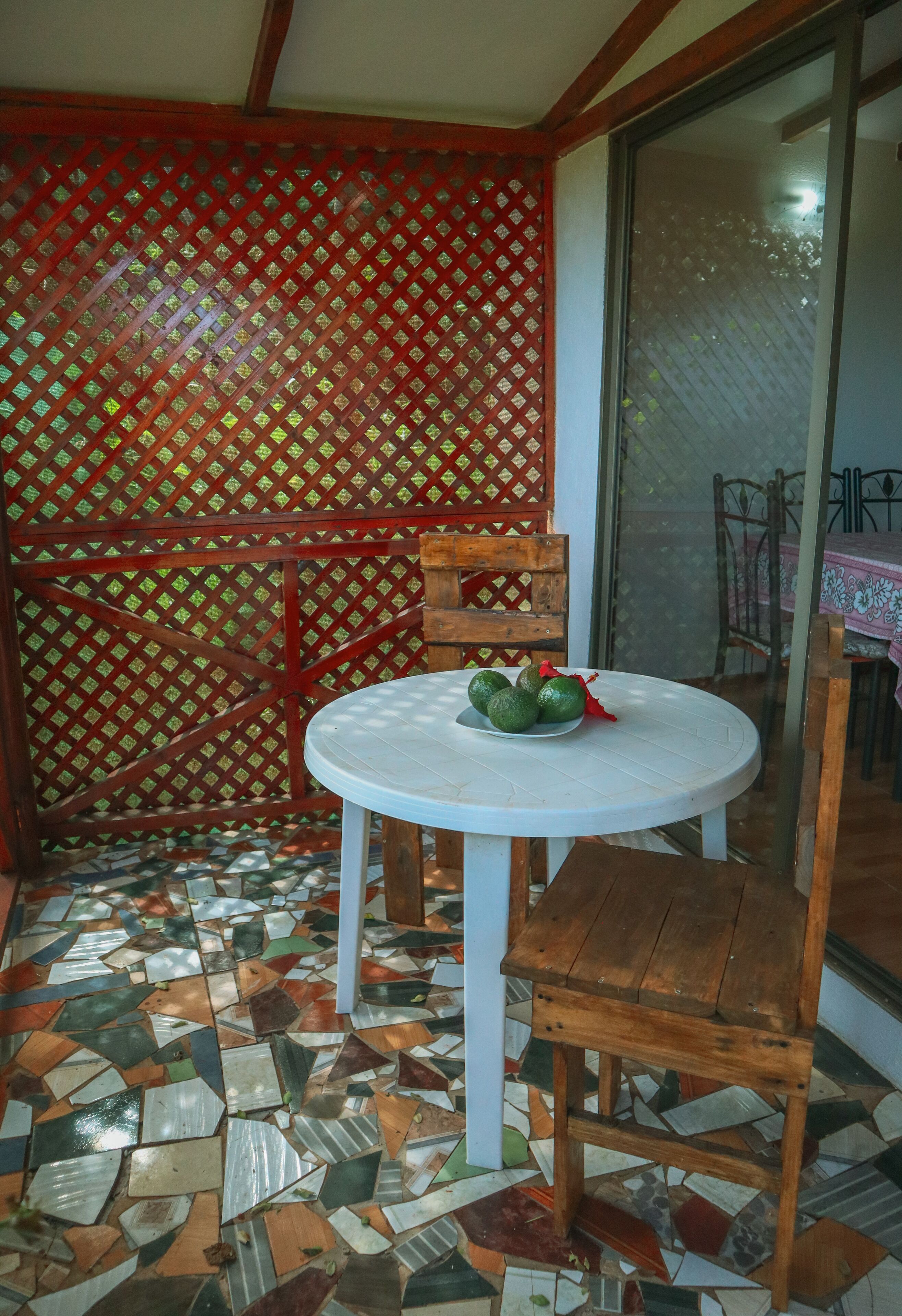 Um quarto com soalho em azulejos, uma mesa redonda com uma cadeira e um separador decorativo em rede vermelha.