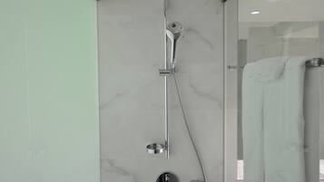 Um banheiro moderno com box de vidro, parede de mármore e uma toalha branca pendurada em um suporte.