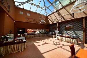 Um quarto amplo com teto alto e claraboia, com um buffet repleto de alimentos e uma área de estar com mesa e cadeiras.