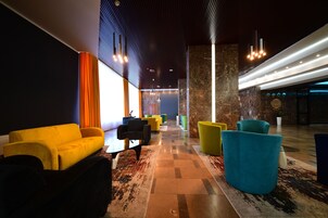 Um lobby moderno com assentos em amarelo vibrante e tons de verde-água, um tapete estampado e uma parede de detalhes em pedra.