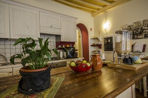 Uma cozinha com armários brancos, uma cafeteira, uma tigela vermelha com frutas e um moedor de café.