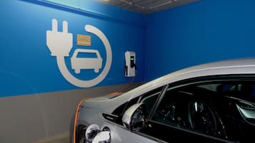 Uma garagem de estacionamento com parede azul, apresentando um ícone de estacionamento e uma estação de carregamento.