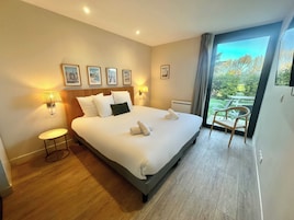 Quarto de hotel com uma cama grande, abajures, uma mesinha e vista para o exterior.