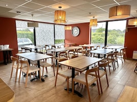 Um restaurante com várias mesas e cadeiras, grandes janelas e painéis decorativos na parede.