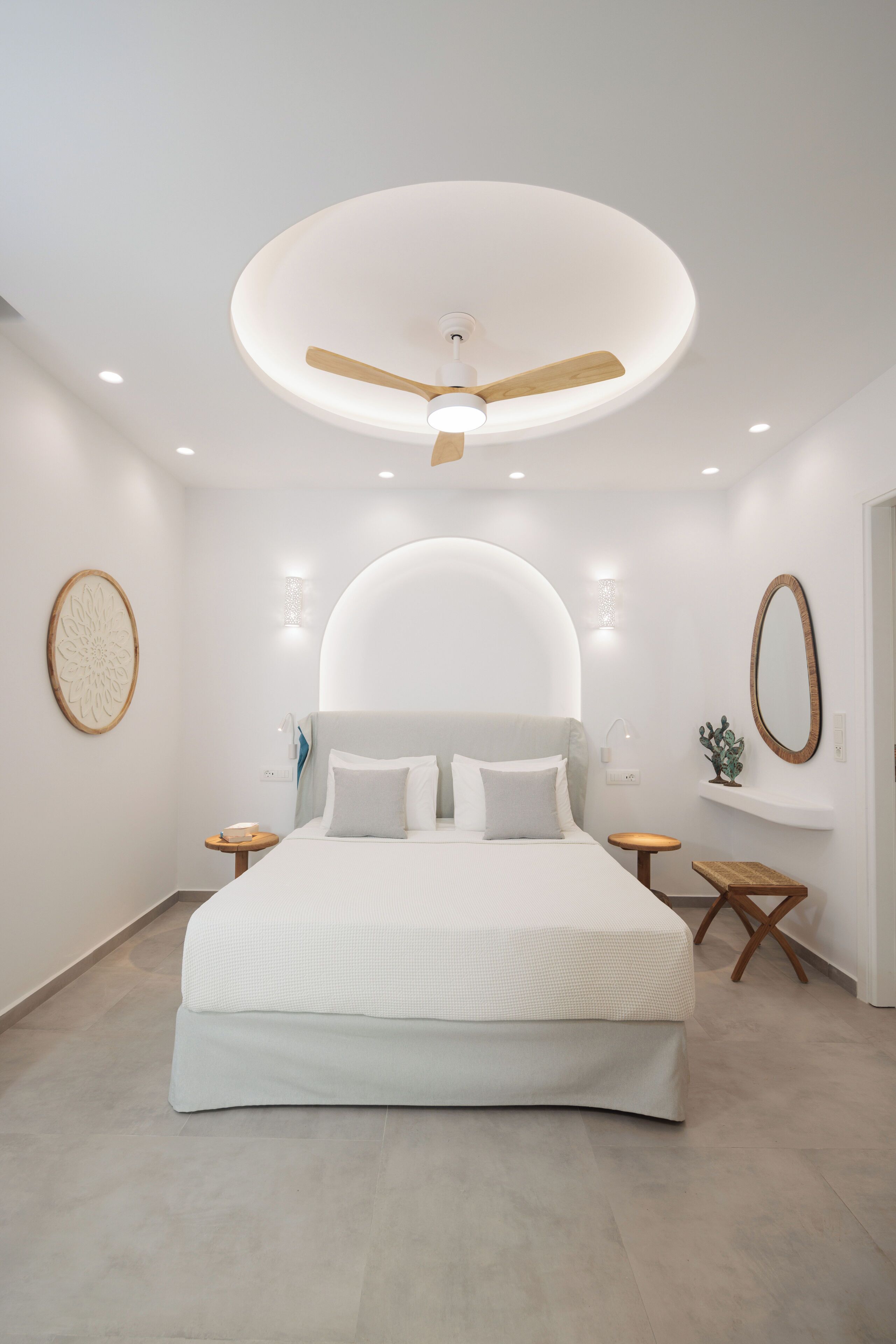 Quarto moderno com uma cama grande, ventilador de teto, iluminação embutida e uma mesinha de cabeceira.
