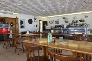Um restaurante com mesas e cadeiras de madeira, um balcão com vitrine e várias decorações nas paredes, incluindo quadros e um barco.