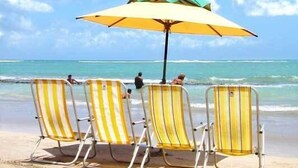 Uma praia com quatro cadeiras de praia listradas e um guarda-sol verde.