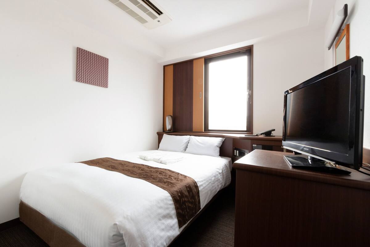 Quarto de hotel com cama, televisão, escrivaninha e janela.