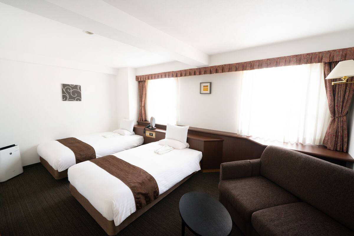 Quarto de hotel com duas camas, um sofá, uma escrivaninha e uma cadeira.